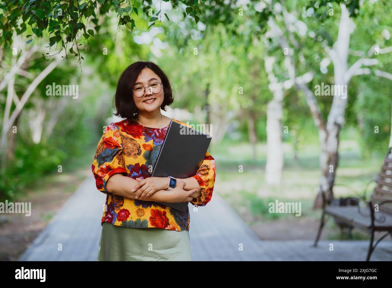A fashionable, smiling Asian woman hugging a laptop is walking in the ...