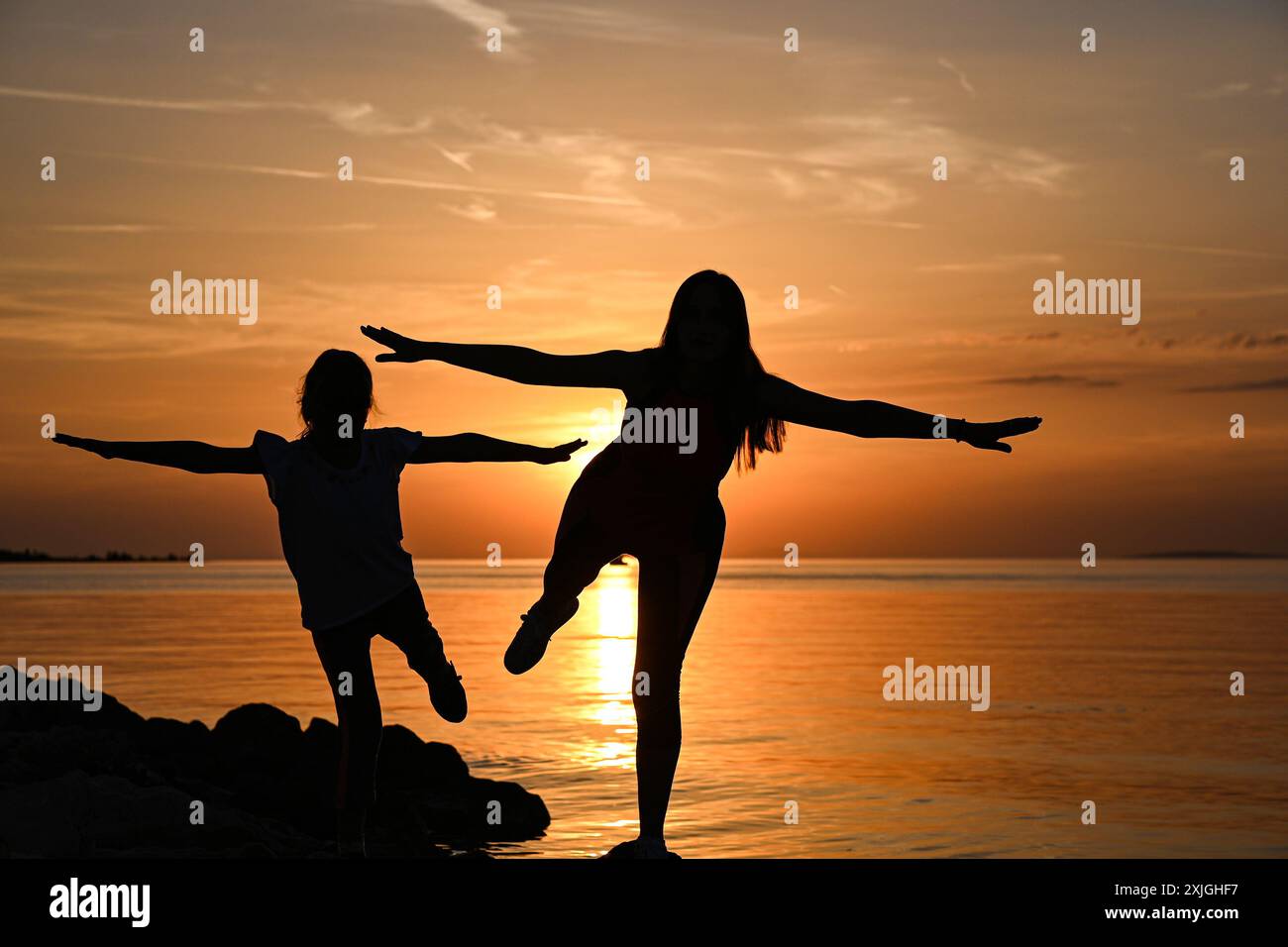 Mother and daughter practicing yoga on the beach at sunset, enjoying a ...