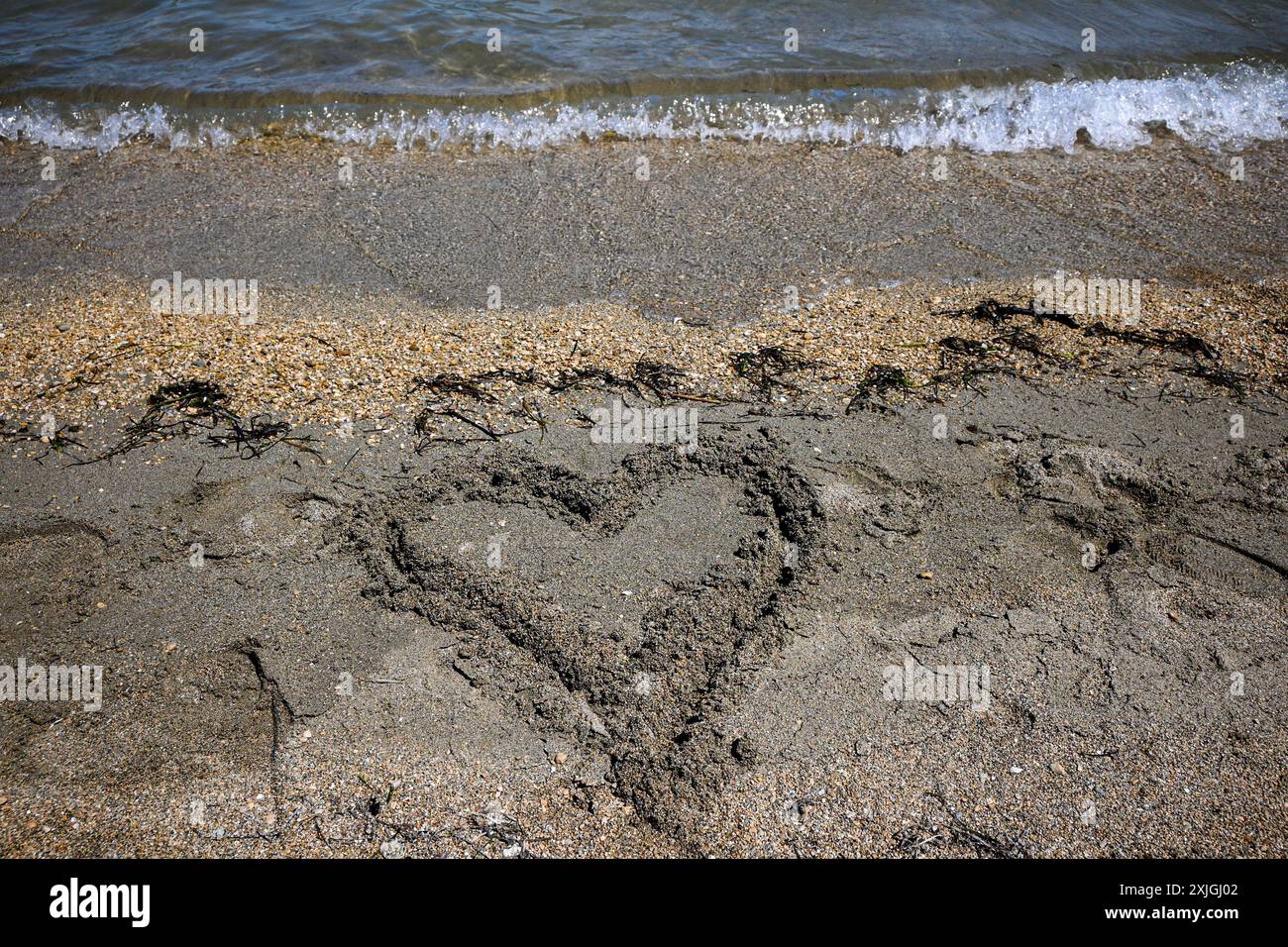 Heart drawn in the sand on a beach being washed away by the ocean waves ...
