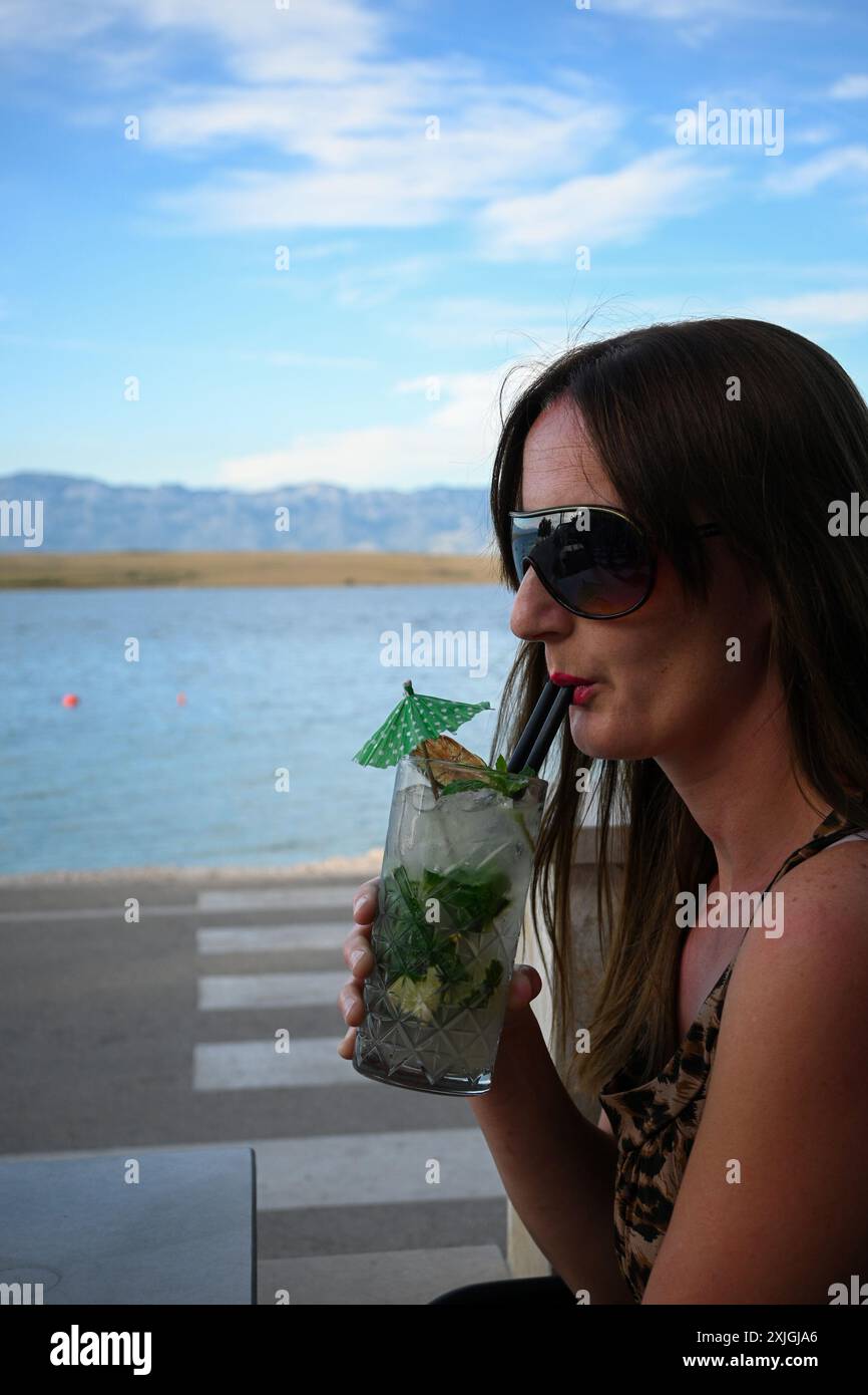 Woman is holding a refreshing mojito cocktail while enjoying the ocean ...