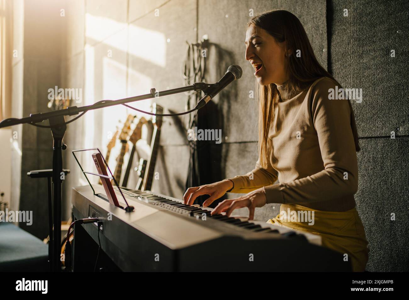 Young woman singing into microphone playing keyboard in music studio ...
