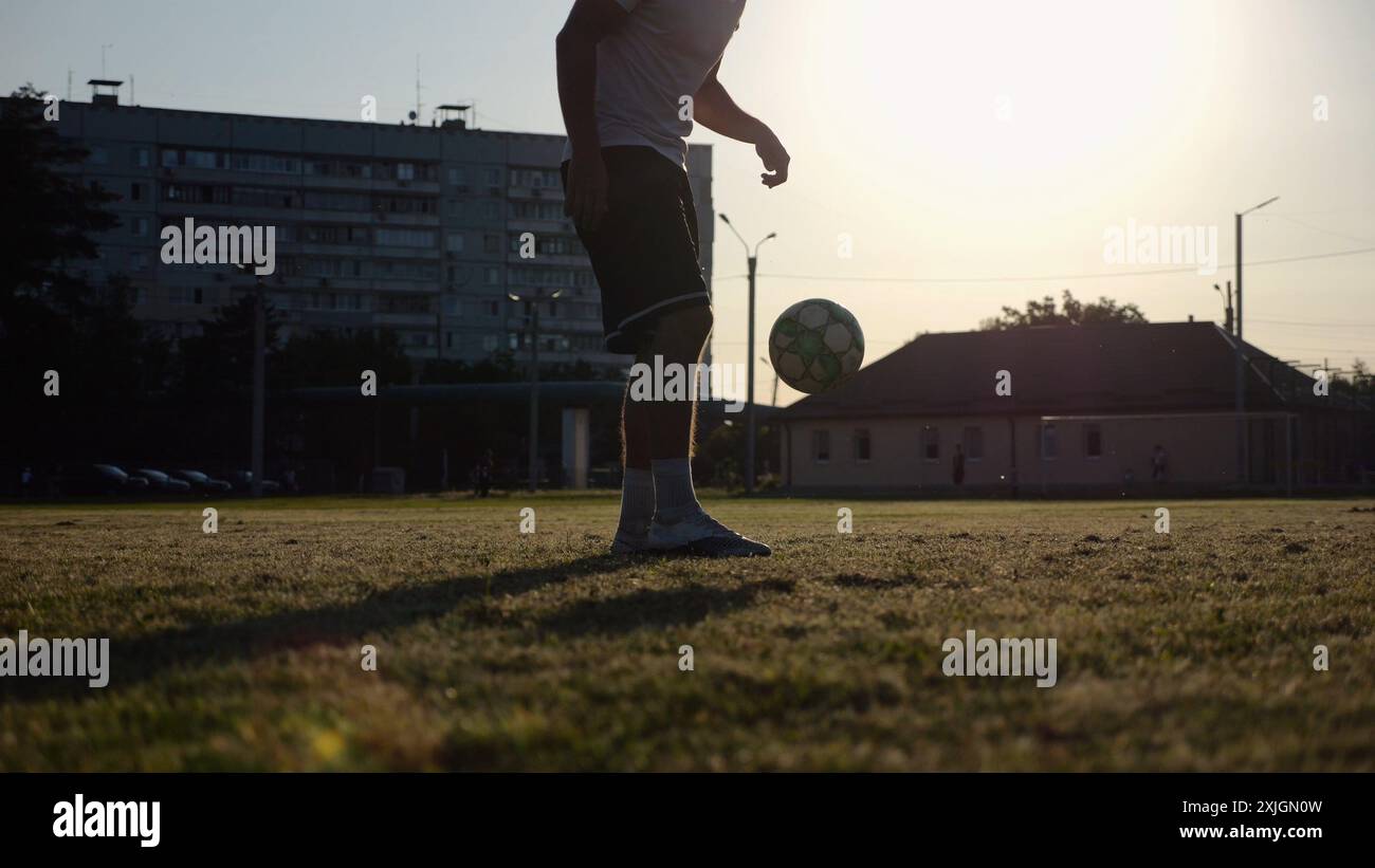 Legs of young man kicking ball at green field. Male feet of ...