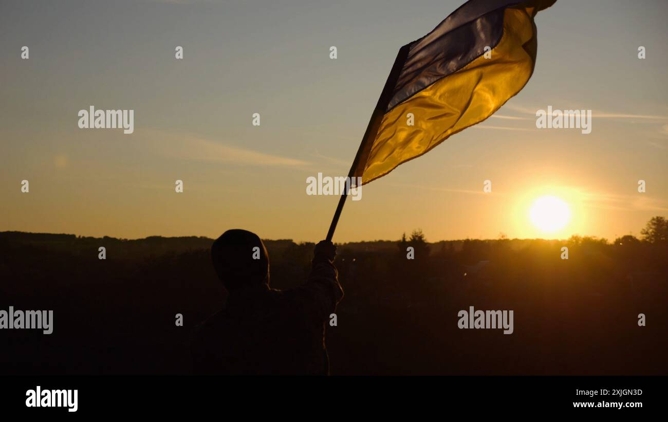 Young man in military uniform waving flag of Ukraine against beautiful ...