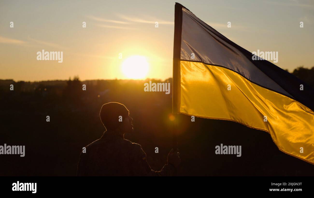 Male soldier stands with raised flag of Ukraine against background of ...