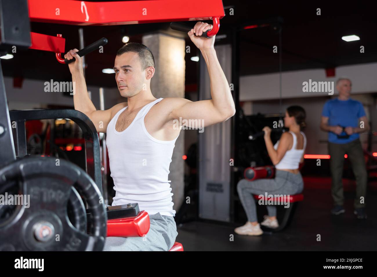 Portrait of man doing triceps curls in exercise machine during strength training in gym Stock ...