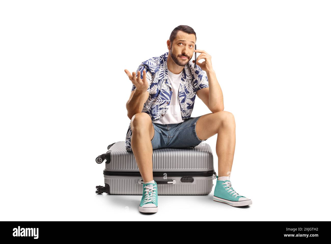 Confused man sitting on a suitcase and using a smartphone isolated on ...
