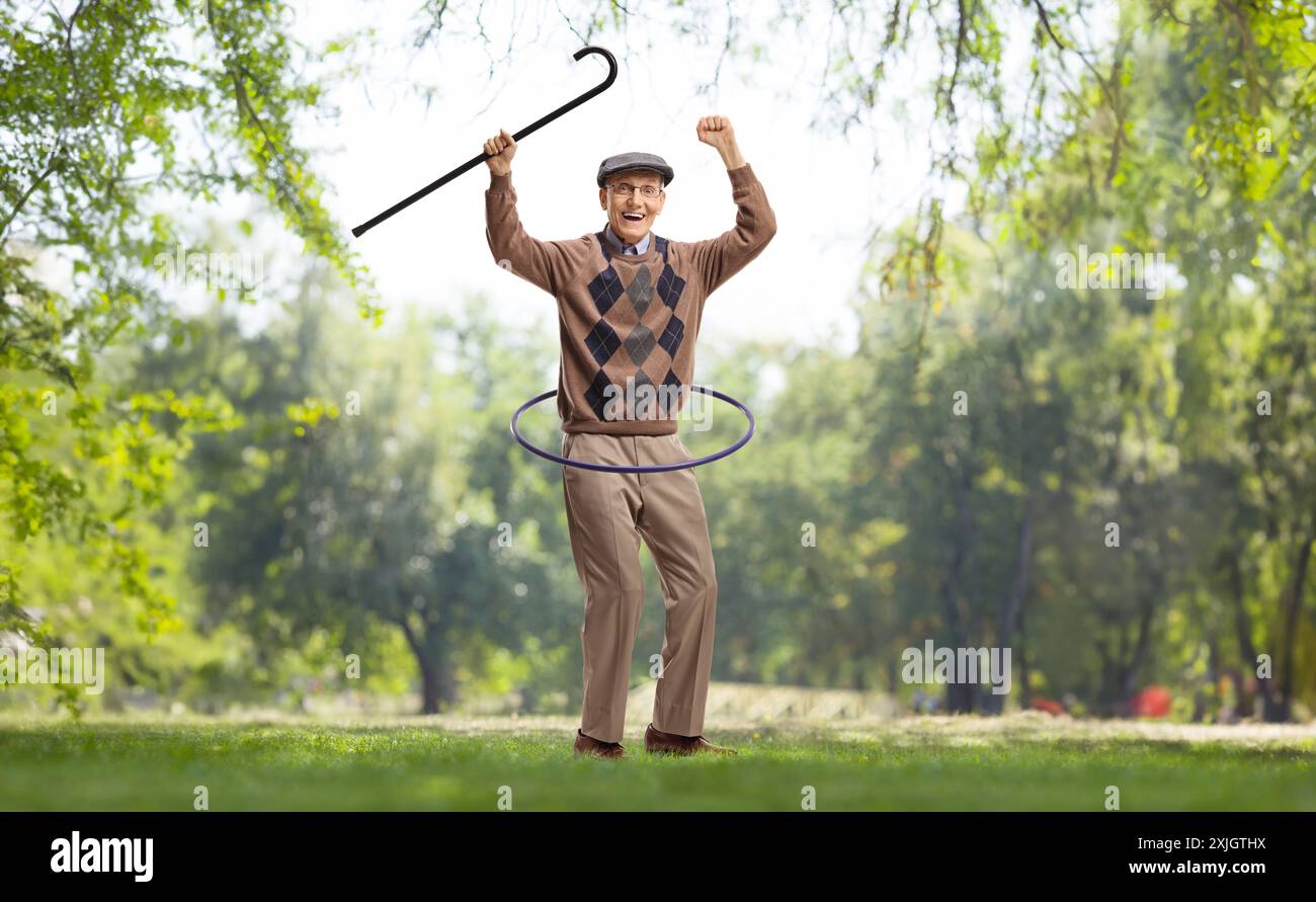 Elderly man holding a walking cane and spinning a hula hoop outdoors in ...