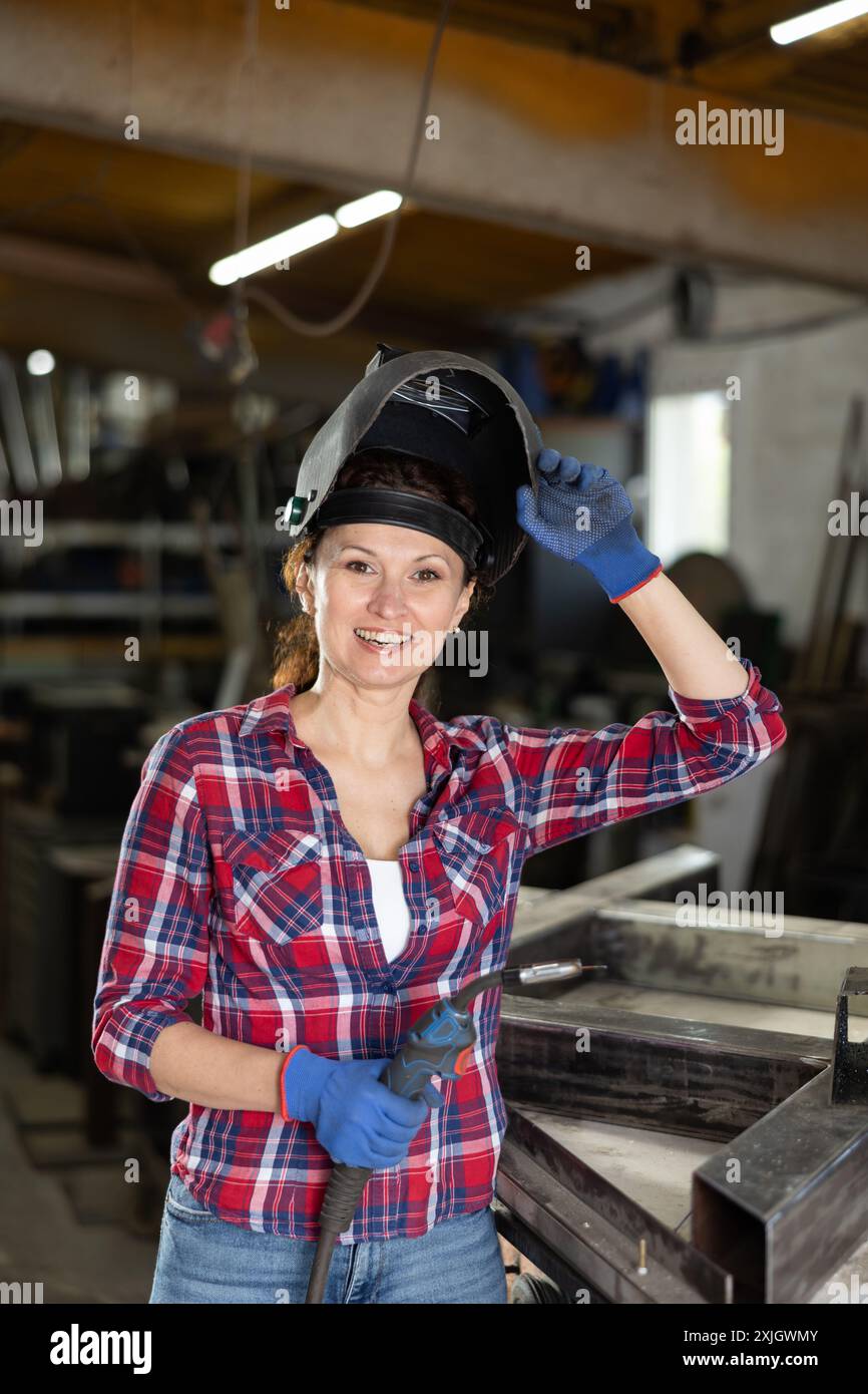Portrait of a female welder standing with a welding semi-automatic machine and a safety helmet ...