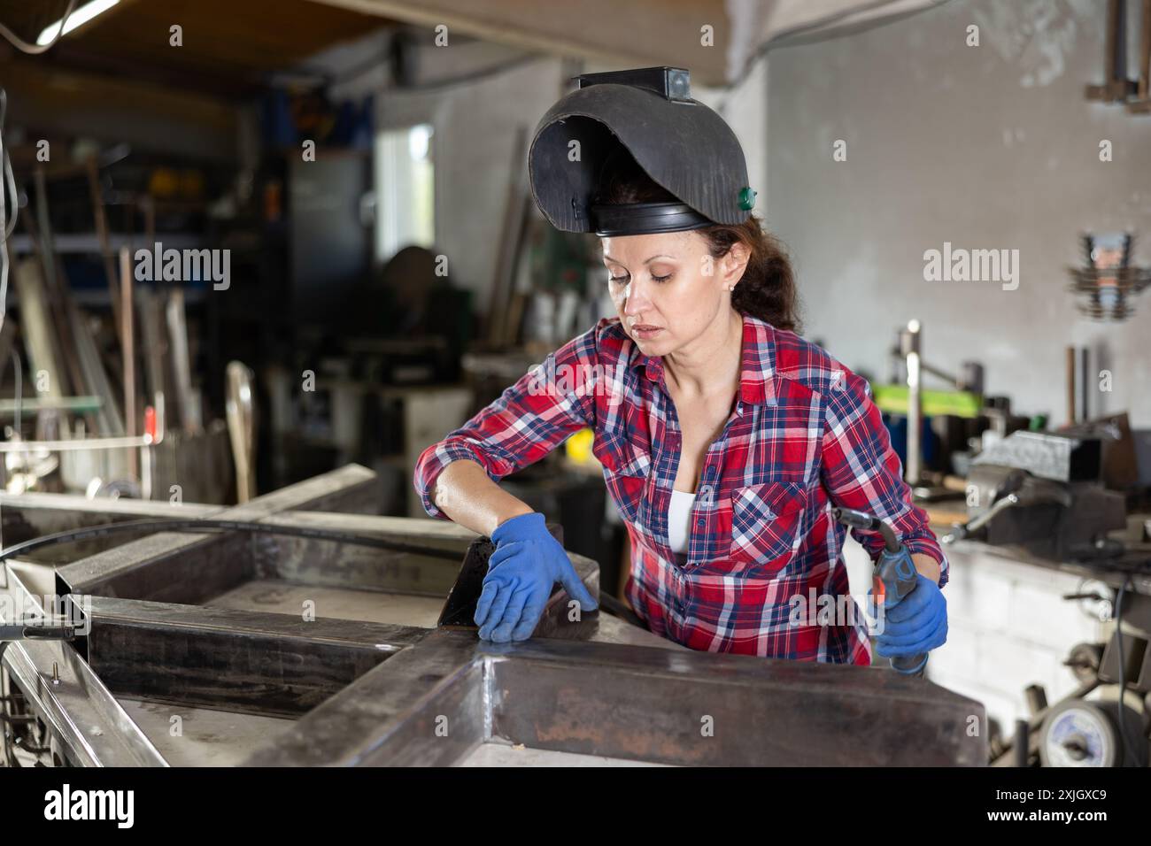 Portrait of a female welder standing with a welding semi-automatic machine and a safety helmet ...