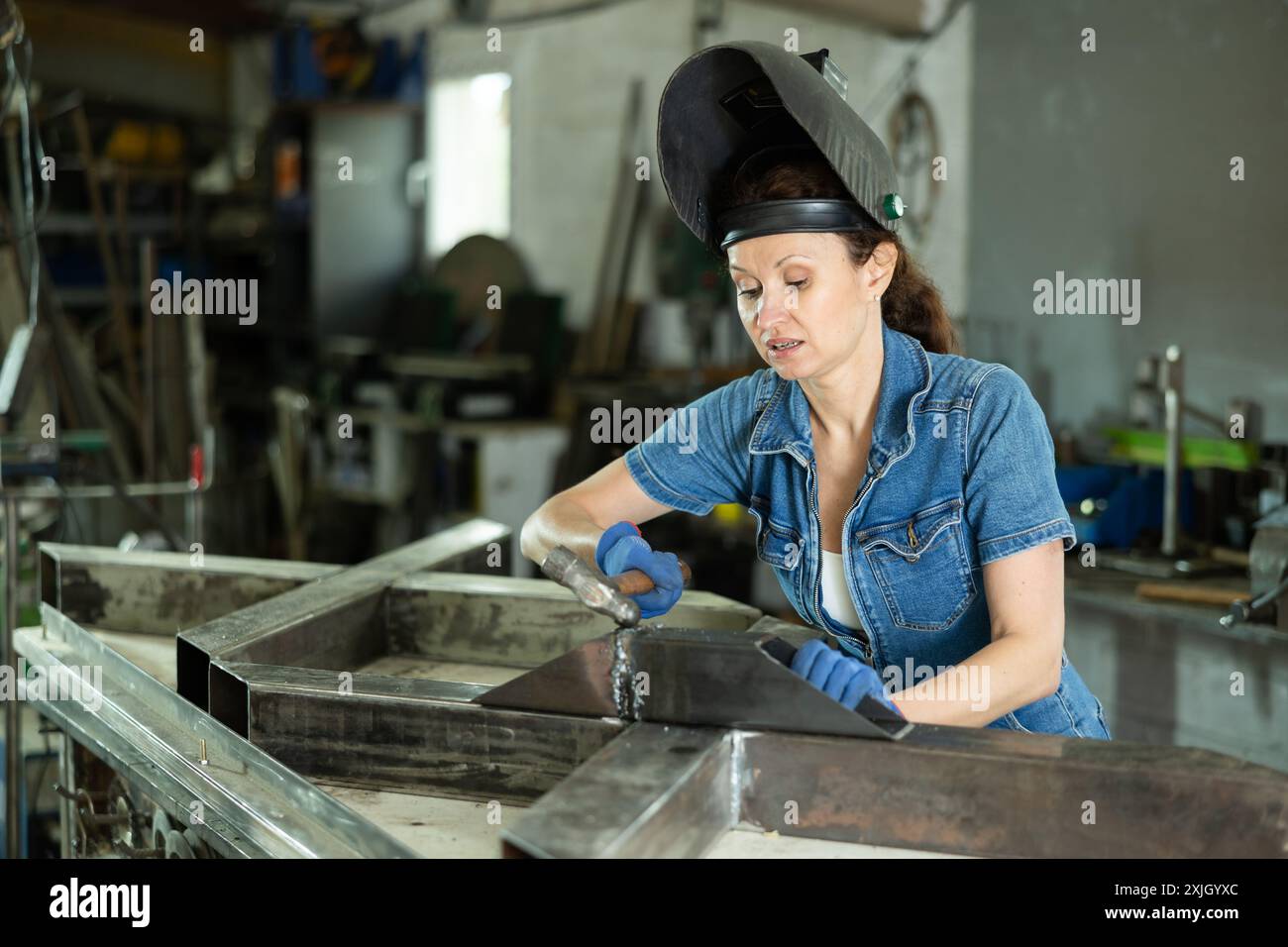 Portrait of a female welder standing with a welding semi-automatic machine and a safety helmet ...