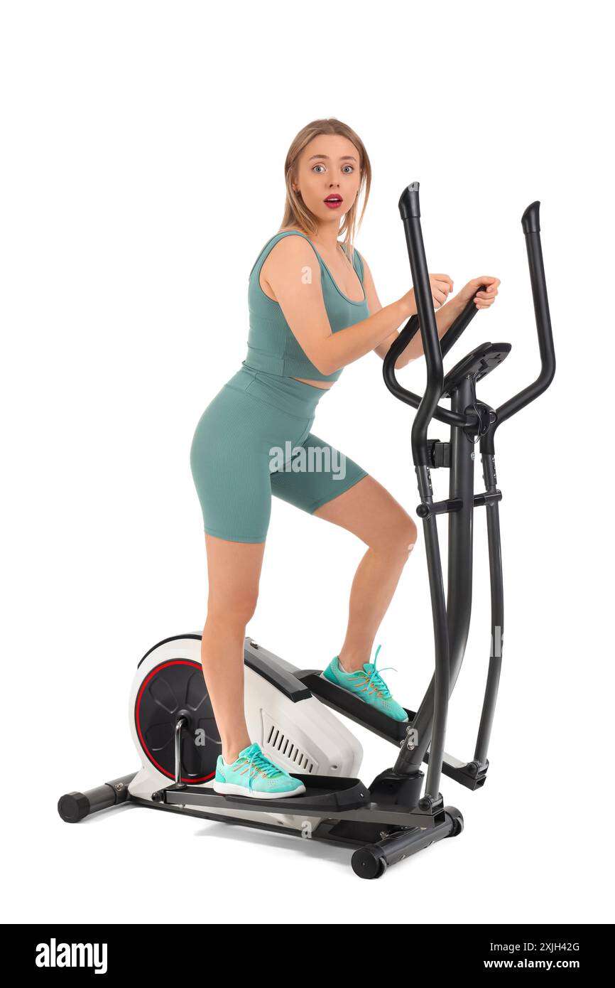 Surprised young woman training on exercising bike against white ...