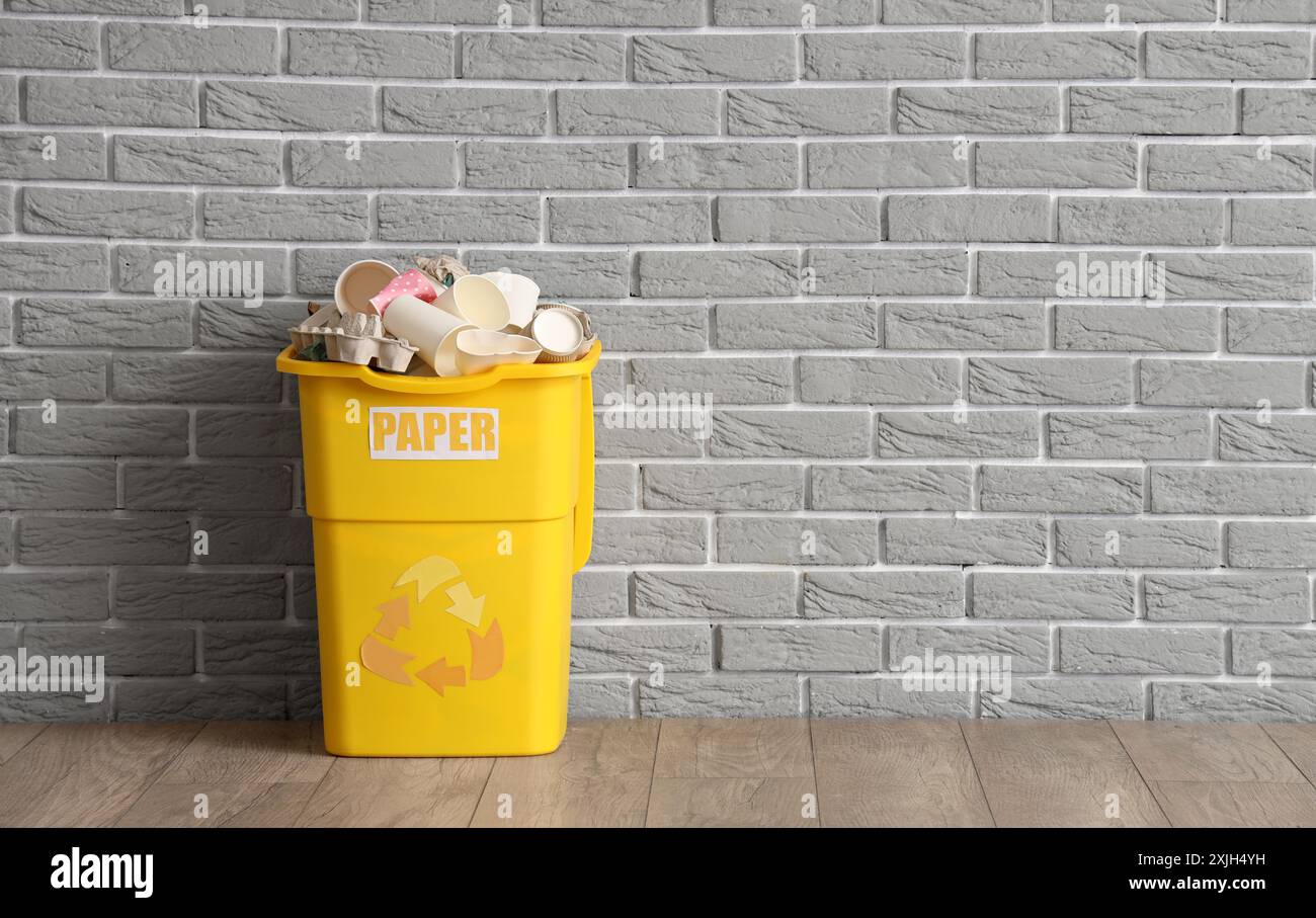 Full trash bin with PAPER sign near grey brick wall. Recycling concept ...