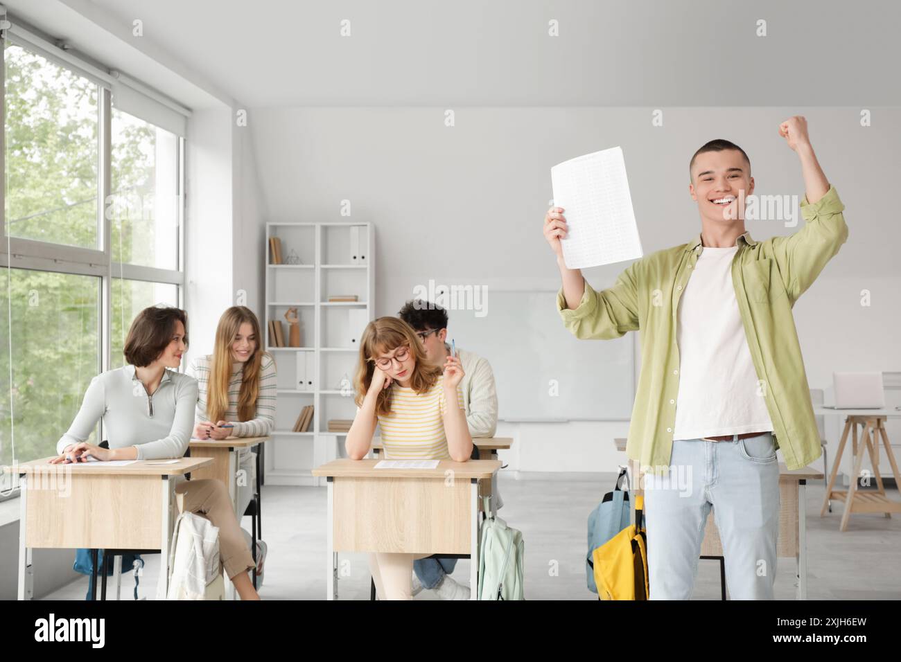Happy male student with answer sheet after exam in classroom Stock ...