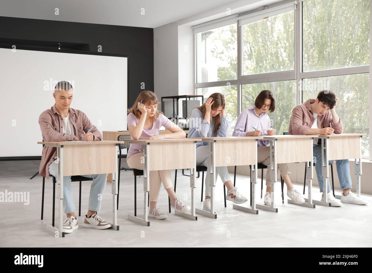 Group of students passing exam at desks in classroom Stock Photo - Alamy