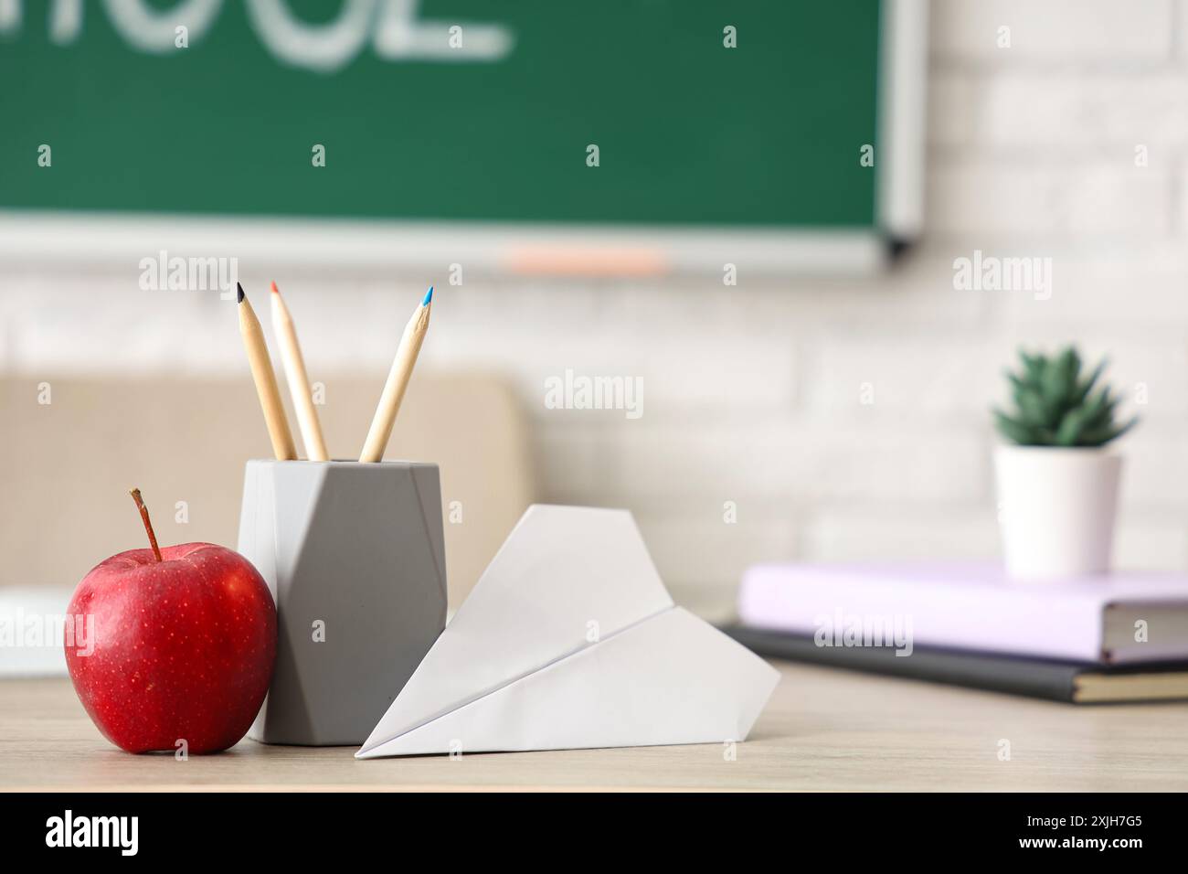 Apple, paper plane and pencils on desk in classroom, closeup. Back to ...
