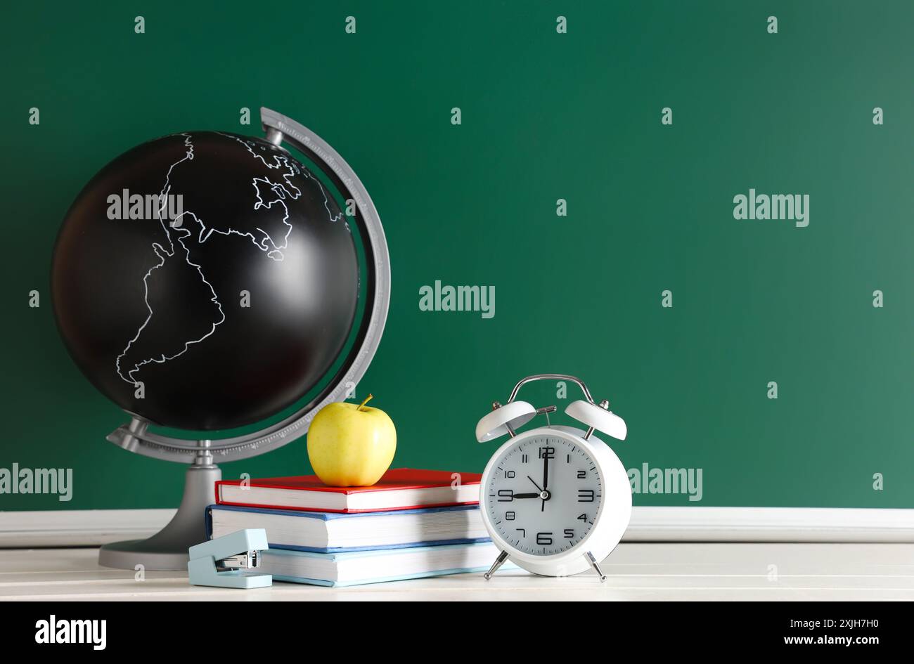 Apple, alarm clock, globe and books on desk near chalkboard. Back to ...