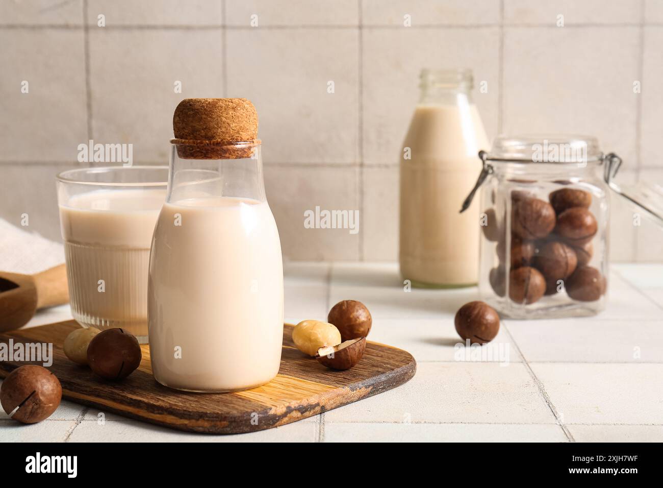 Glass and bottles of fresh macadamia milk on white tile background ...