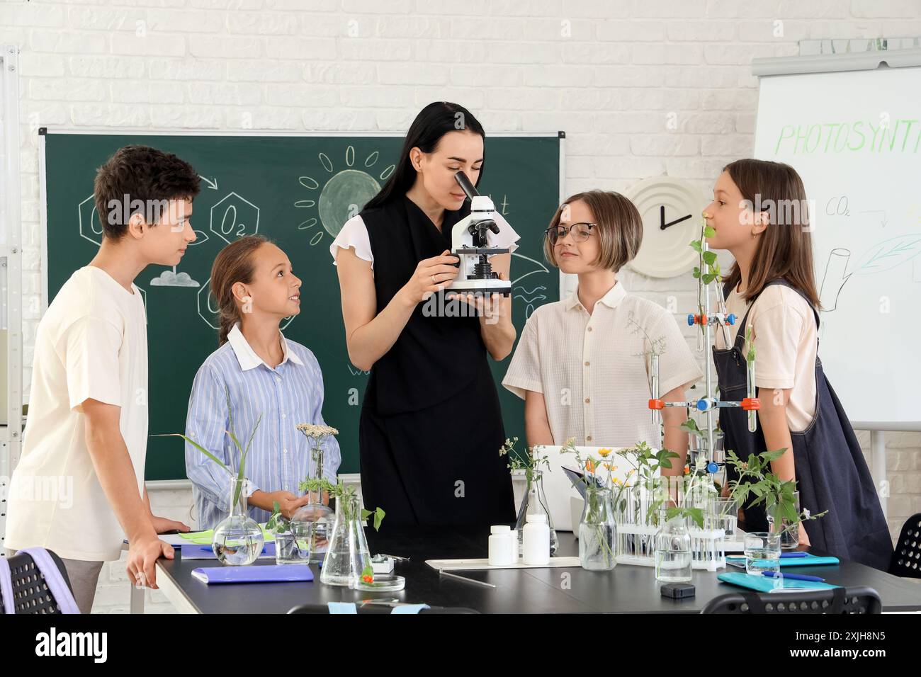 Female teacher with pupils looking through microscope in Biology class ...