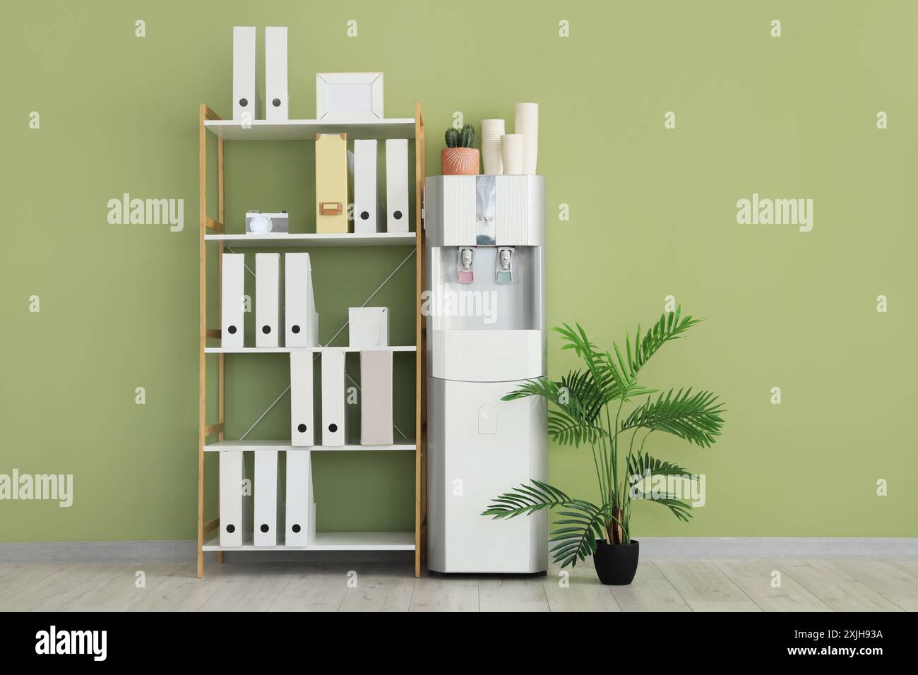 Modern water cooler with paper cups and shelf unit near green wall in ...
