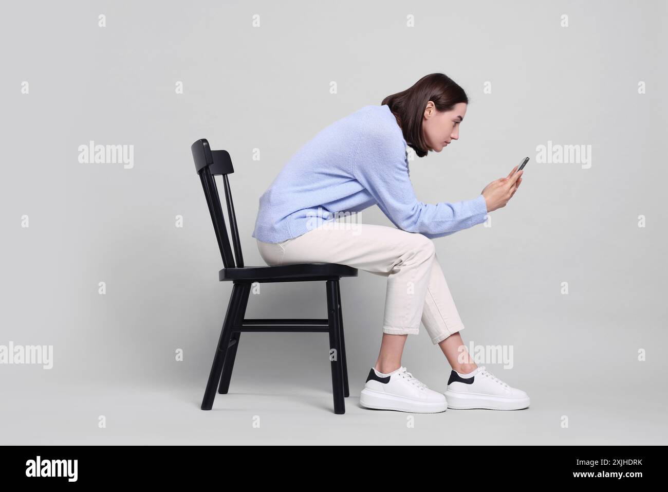 Woman with poor posture sitting on chair and using smartphone against ...