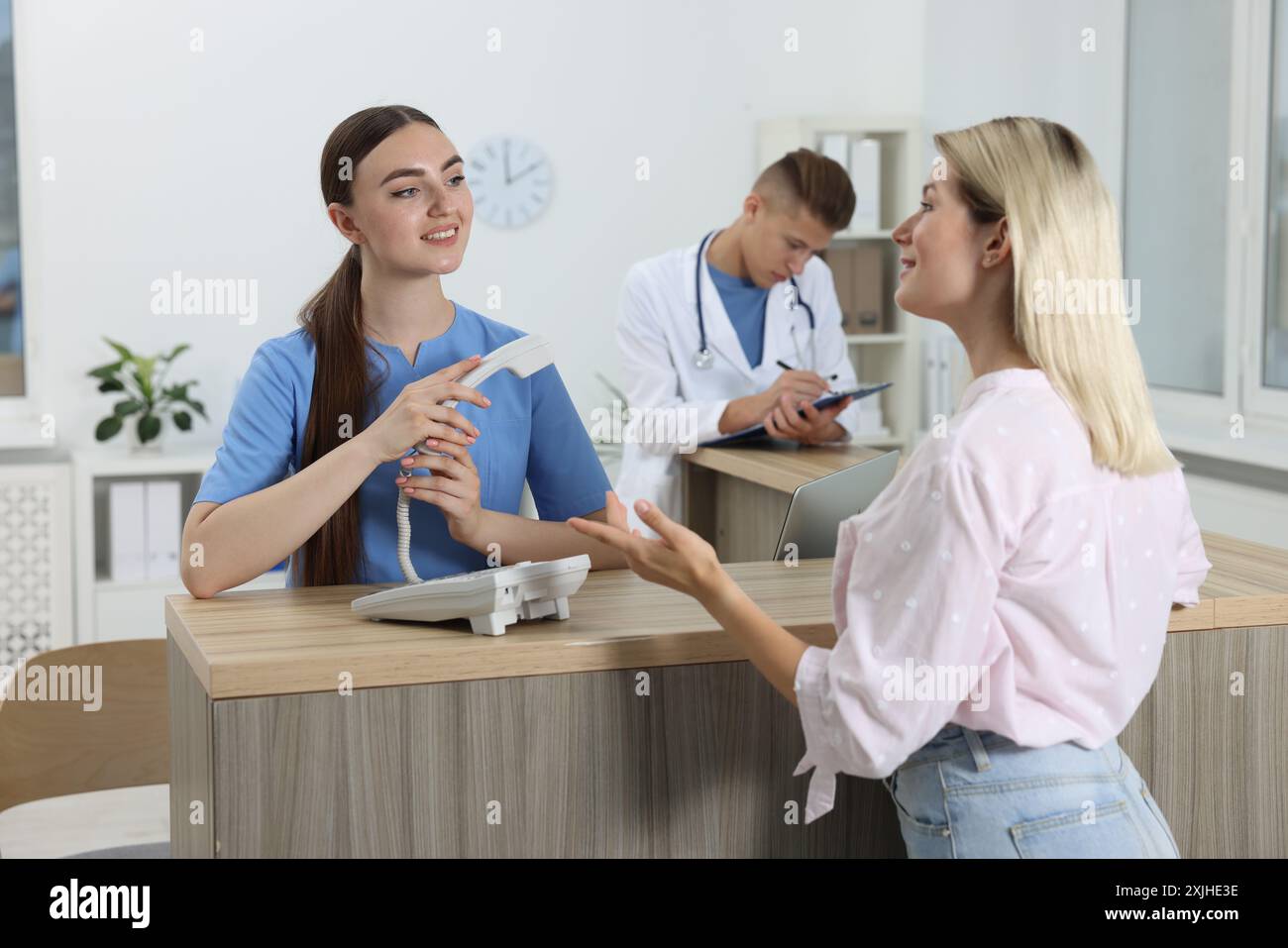 Professional receptionist and doctor working with patient at wooden ...