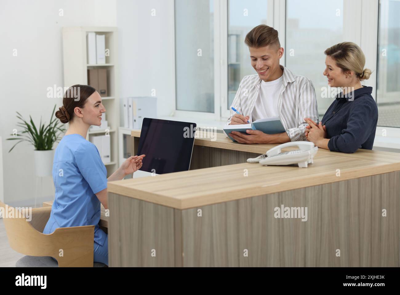 Professional receptionist working with patients at wooden desk in ...
