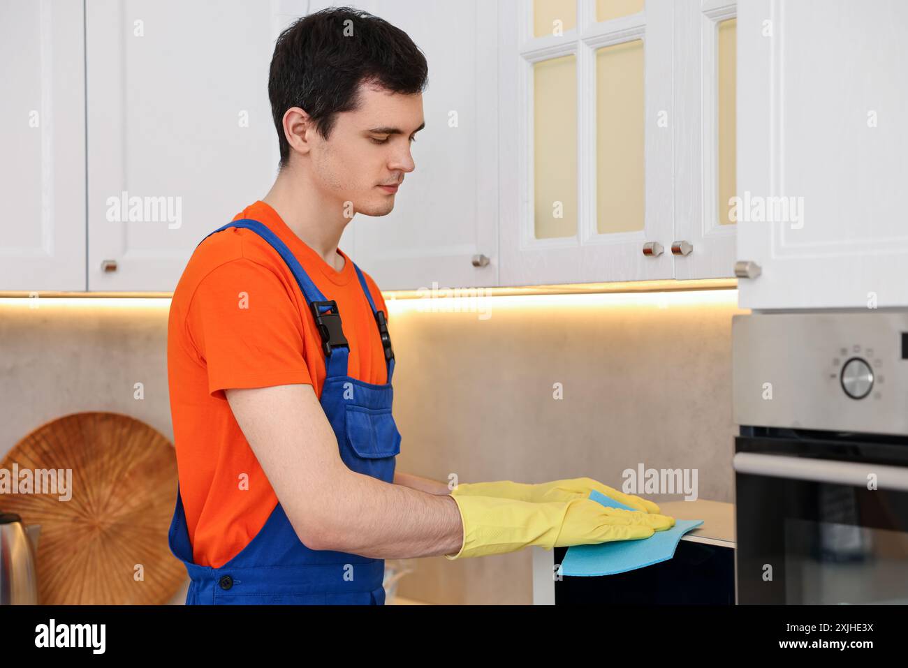 Professional janitor wearing uniform cleaning microwave oven in kitchen ...