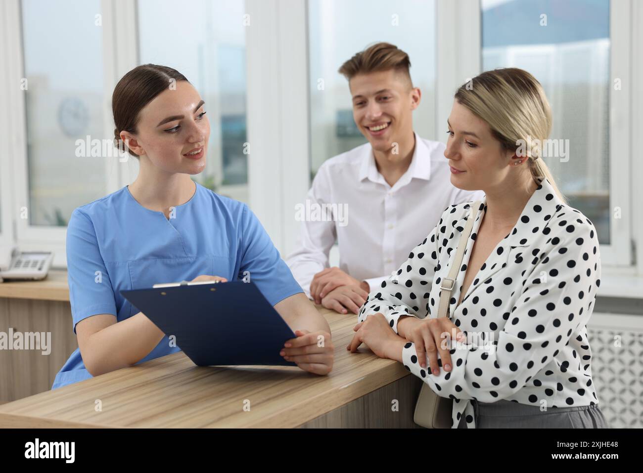 Professional receptionist working with patients at wooden desk in ...