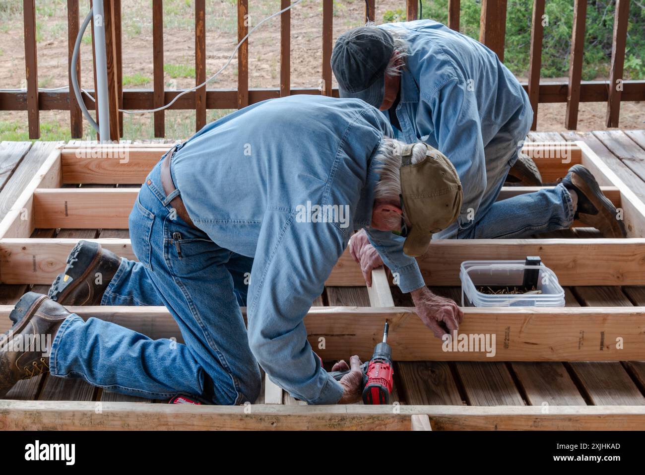 Two senior men, in their 80s, on their knees building a wooden frame ...