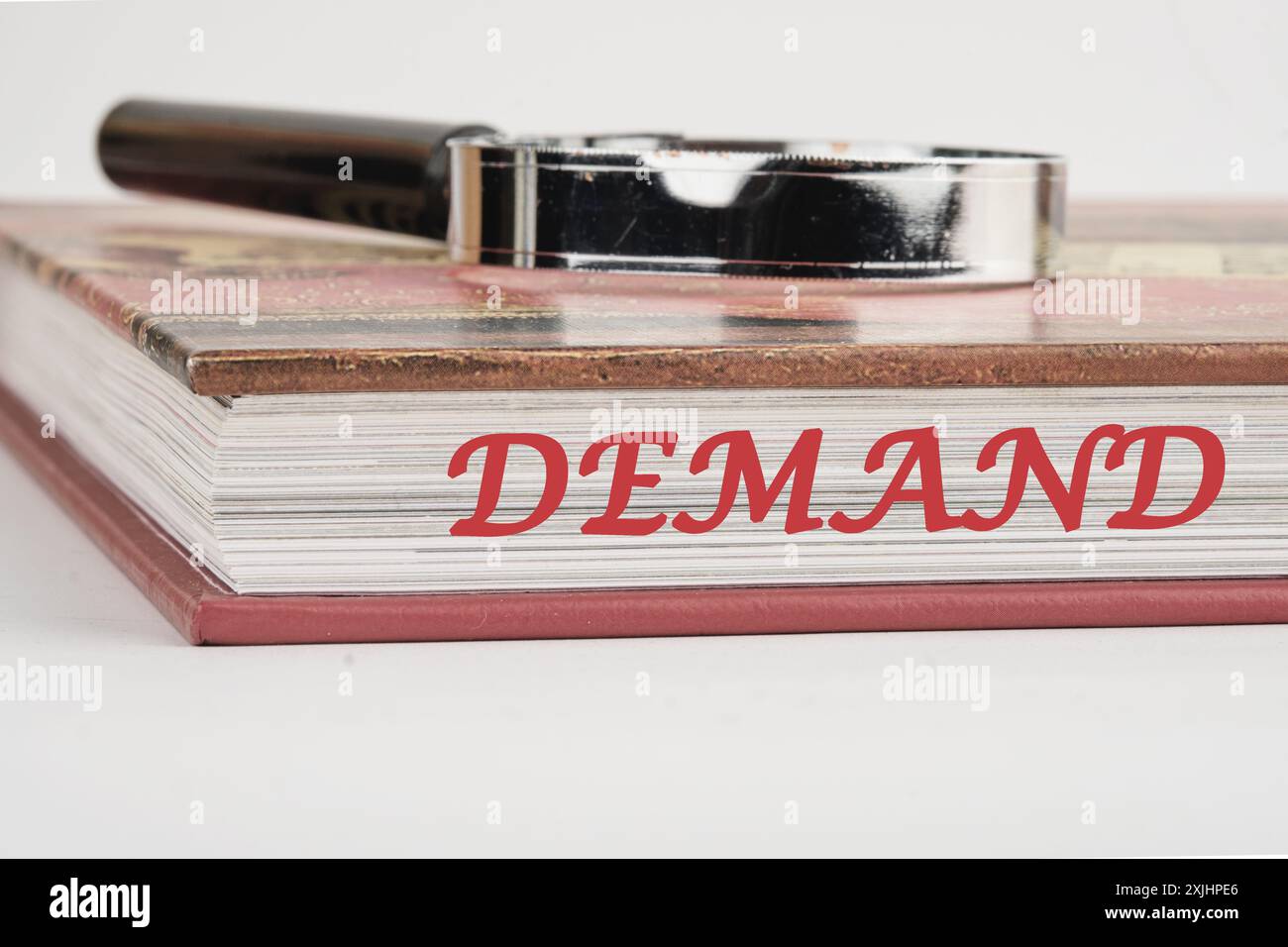 Concept word DEMAND on the end of the book with a magnifying glass on ...