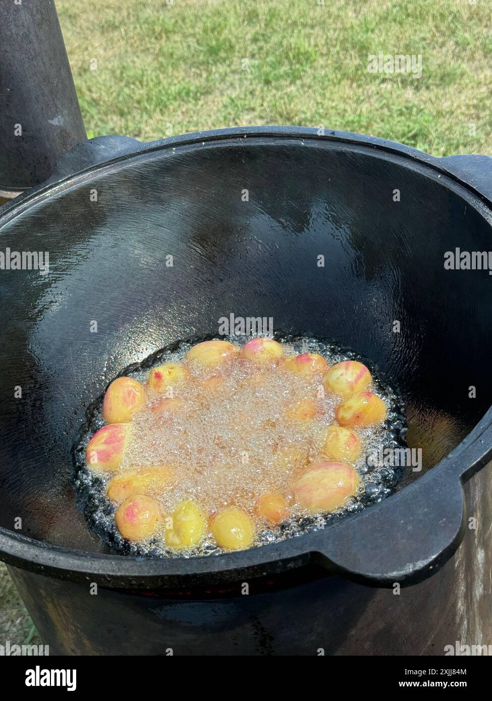A man fries potatoes in oil on a hot grill. Brazier on an open fire ...