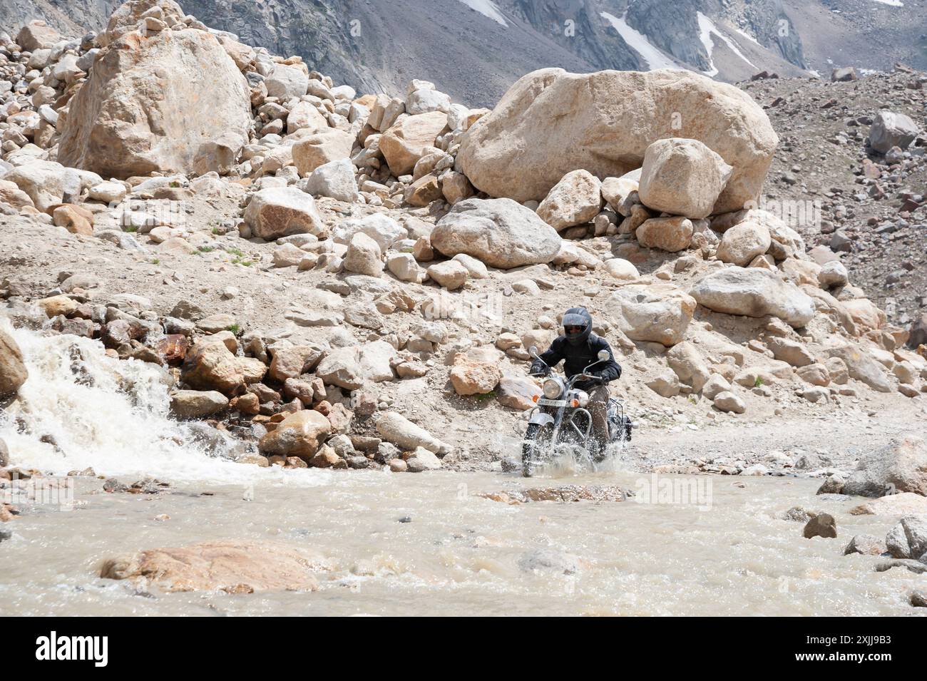 Foreign tourist riding a motorbike through a river with large rocks in ...