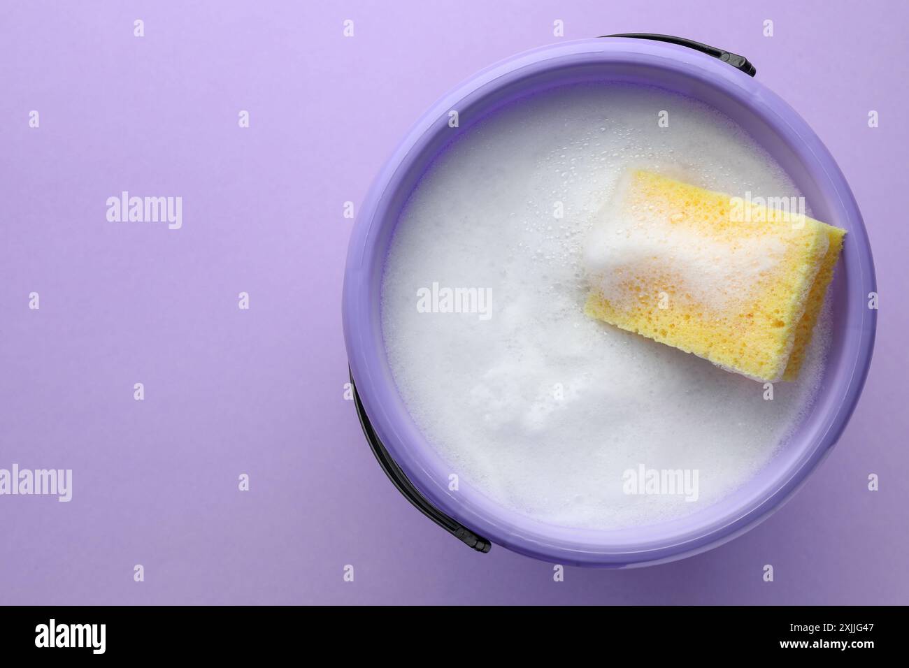 Bucket with foam and sponge on violet background, top view. Space for ...