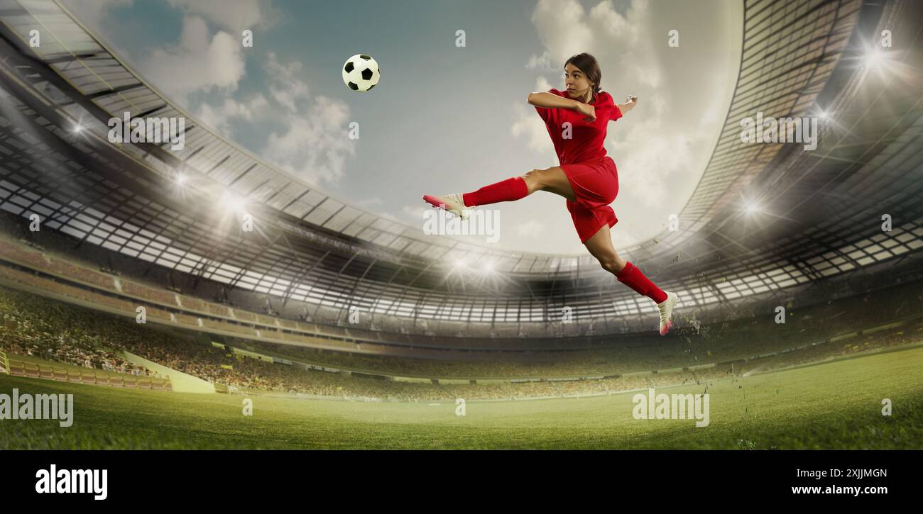 Female soccer player in red performs high jump kick on stadium field. Arena packed with ...