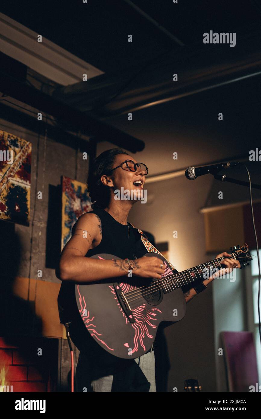 Young woman sings into a microphone and plays a guitar in a club Stock ...