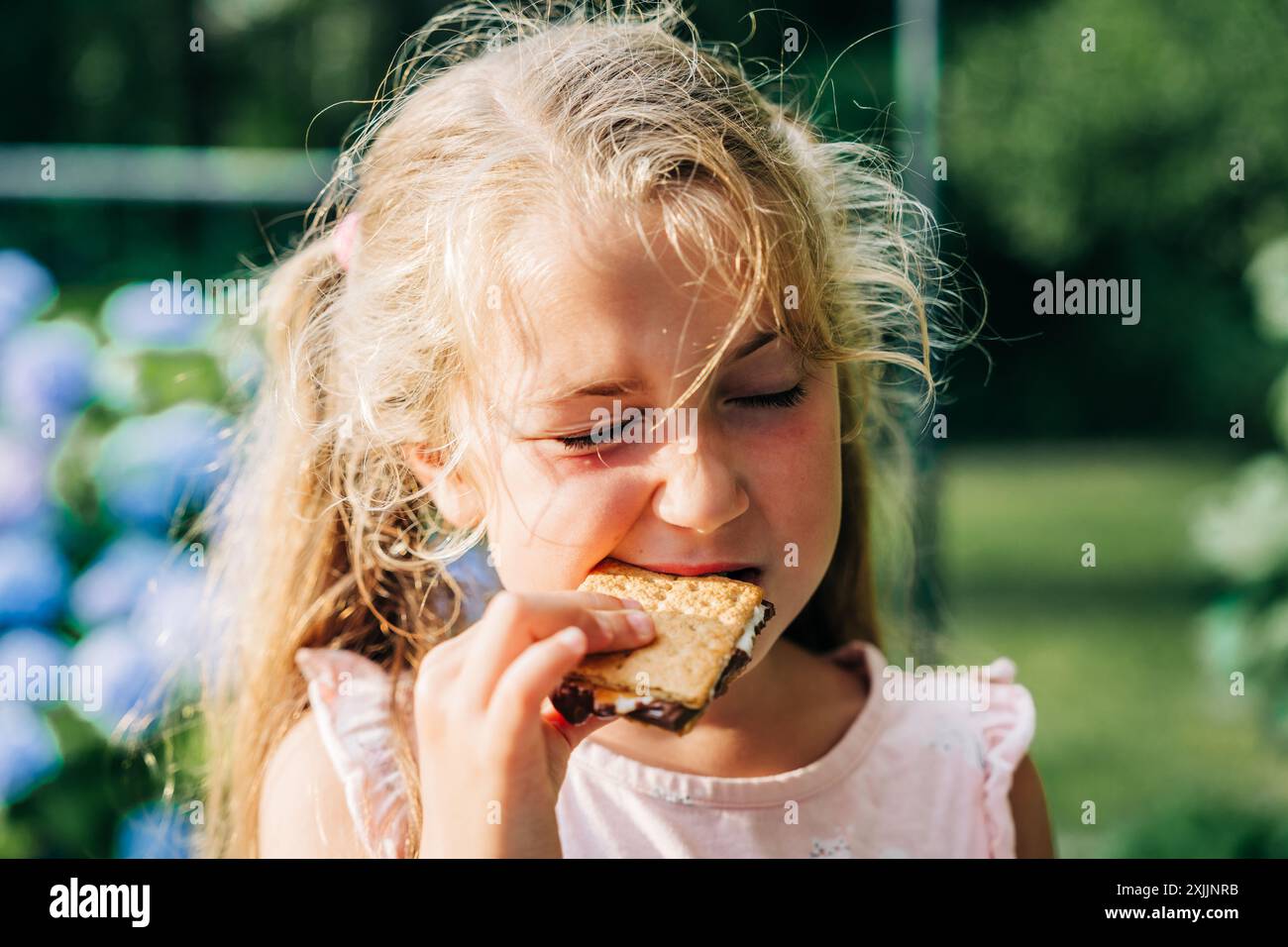 Young girl enjoying a s'more in an outdoor setting with flowers Stock ...
