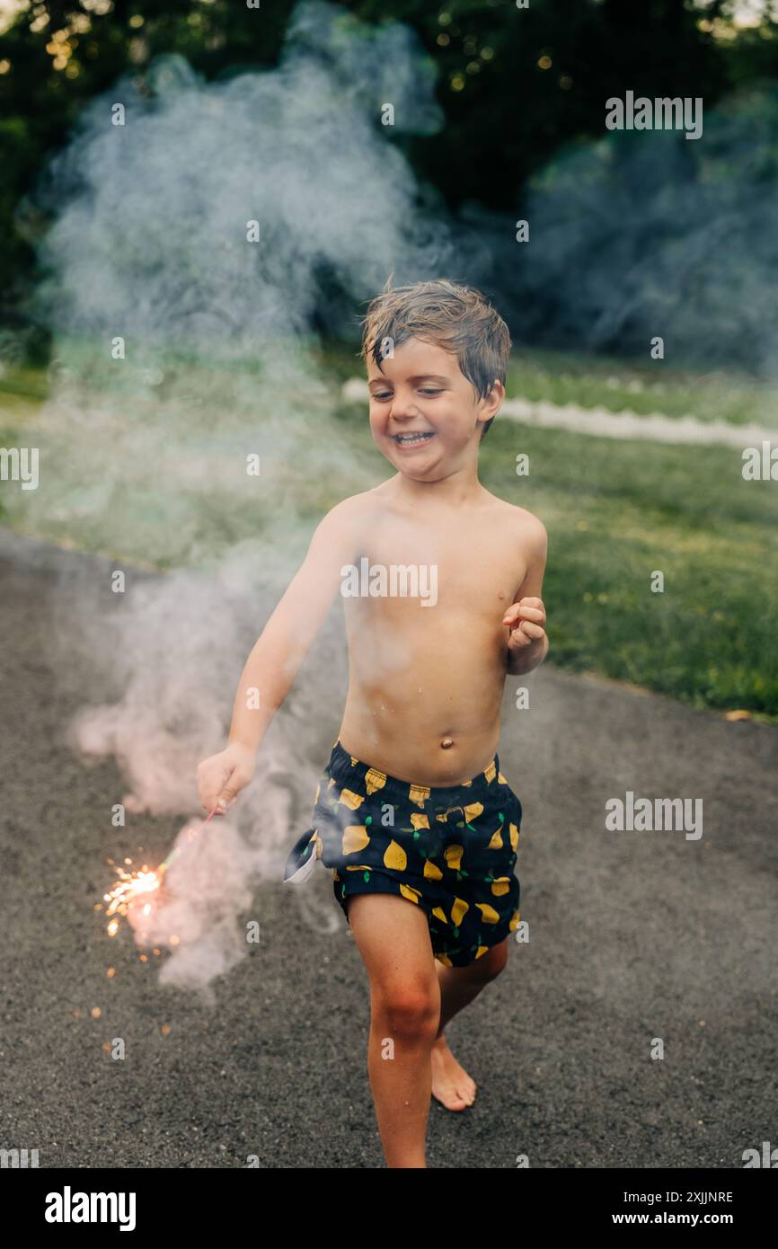 Shirtless young boy running and playing with sparklers in a driveway ...
