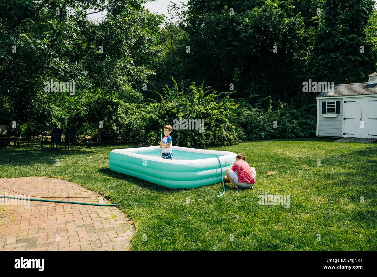 Two kids playing in an inflatable pool in a green backyard Stock Photo ...