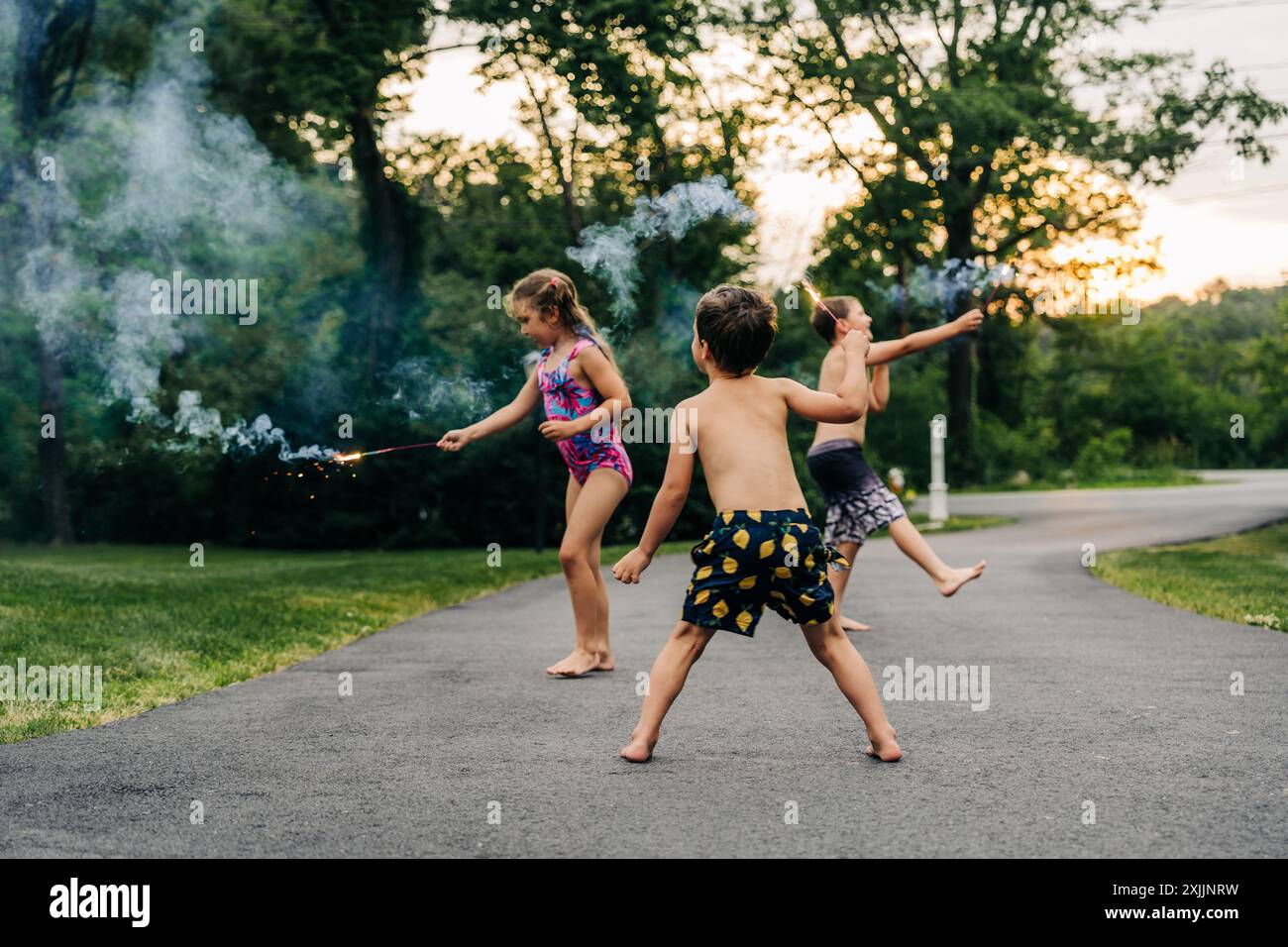 Three kids playing with sparklers on a driveway at sunset Stock Photo ...