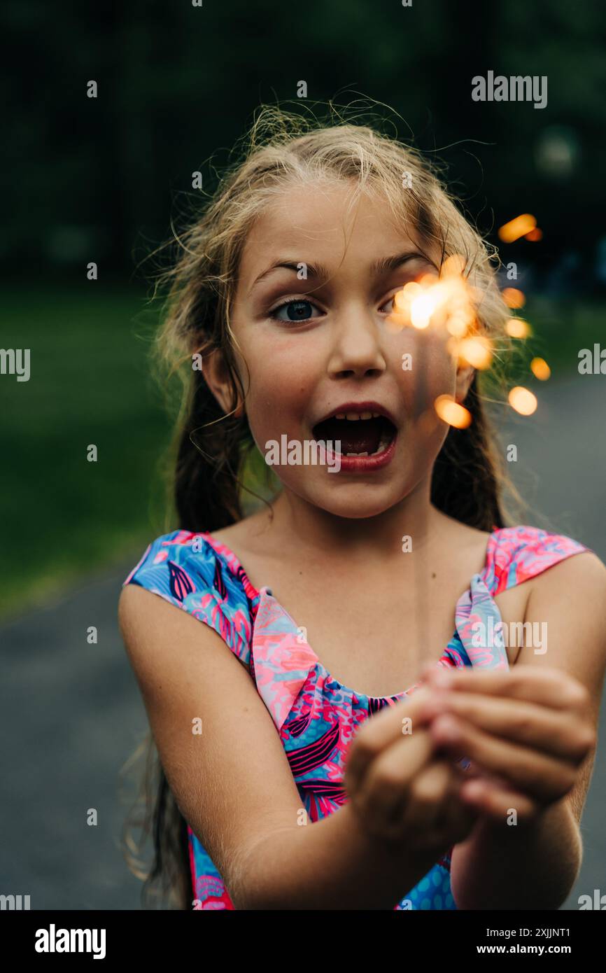 Girl holding a lit sparkler, surprised expression, colorful swimsuit ...
