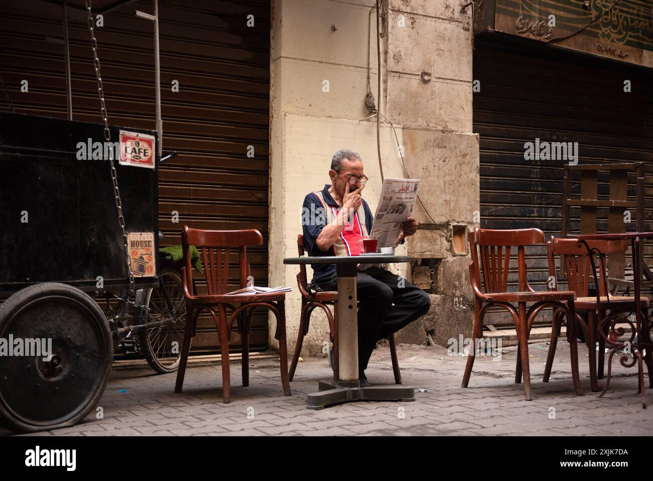Cairo, Egypt. 14th June, 2024. An Egyptian man smokes, drinks tea, and reads a newspaper in a ...