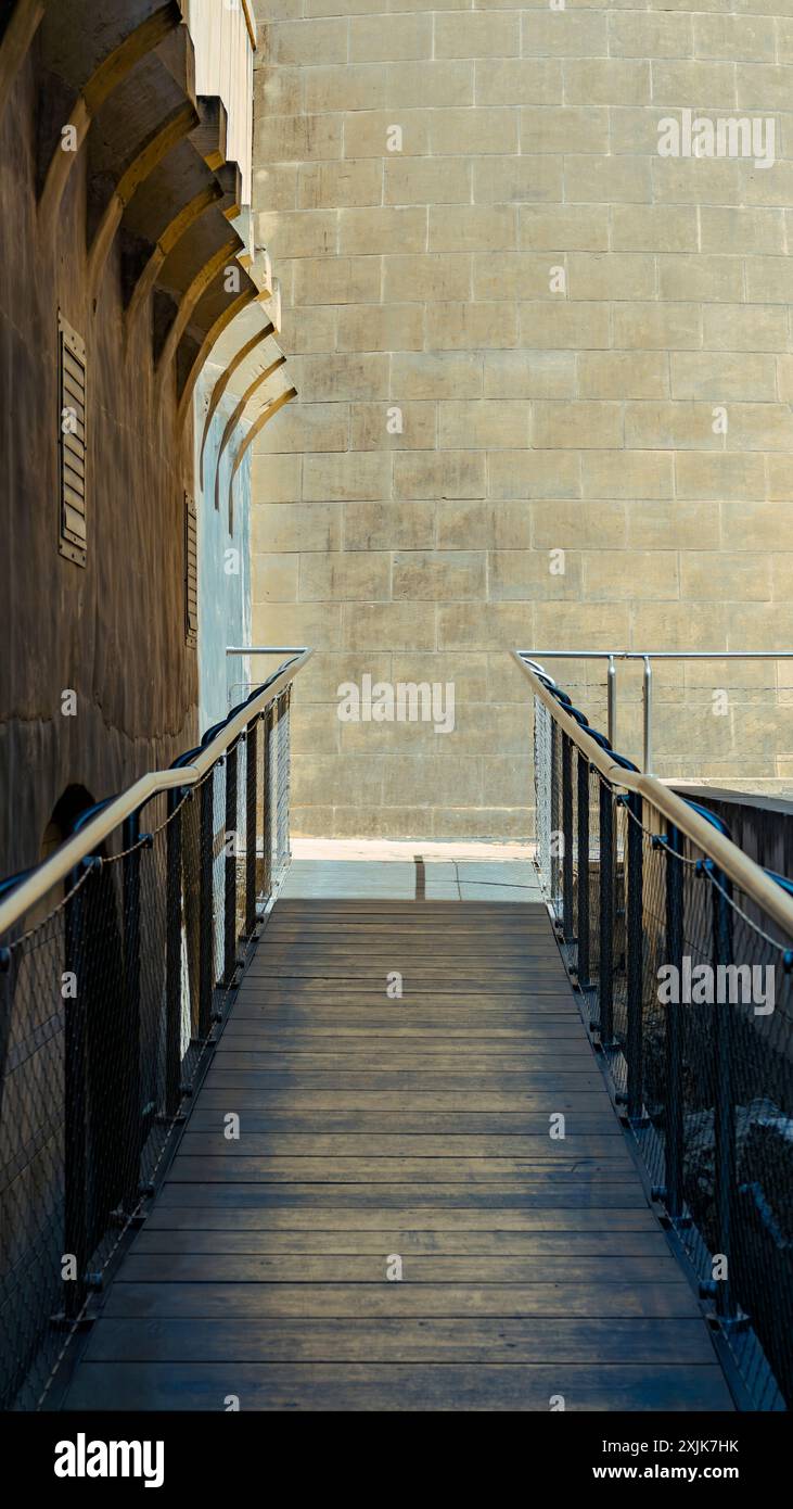 Shadowed walkway of an industrial pedestrian bridge with metal railings ...