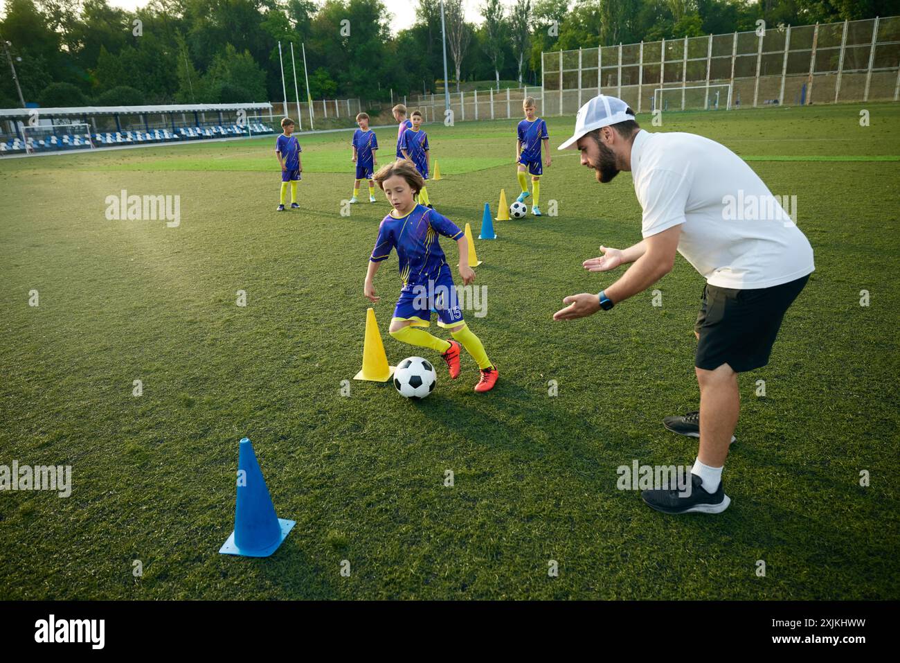 Boy practices dribbling through cones with focused encouragement from ...