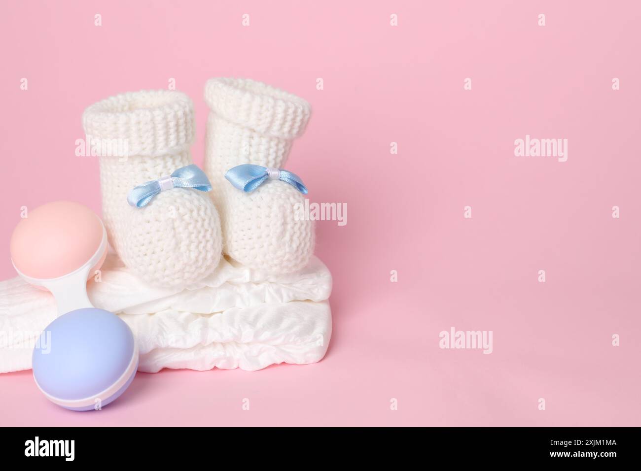 Baby rattle, booties and diapers on pink background. Space for text ...
