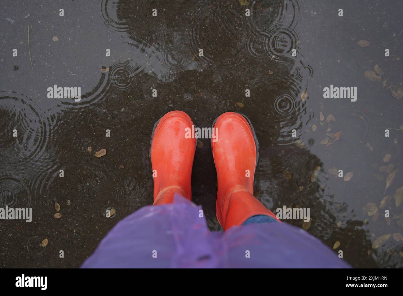 Woman wearing red rubber boots standing in rippled puddle, top view ...