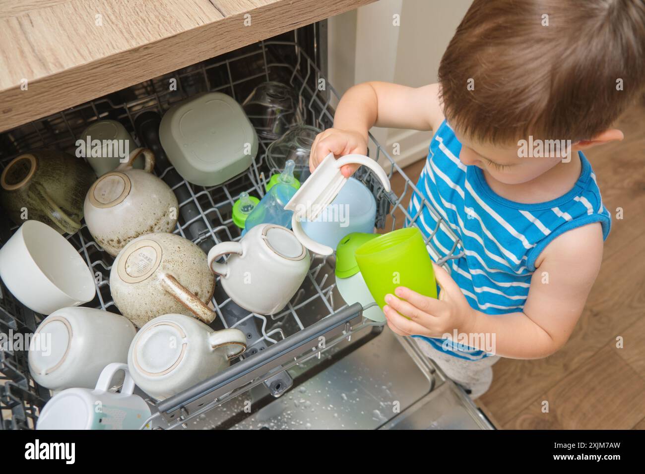 Young child loading dishwasher with various dishes. Indoor lifestyle ...