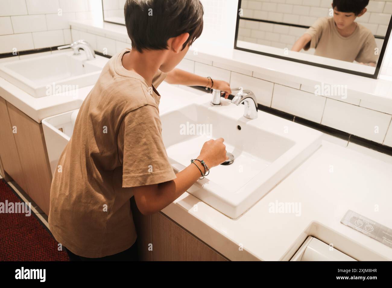 Asian boy washing his hands in front of a mirror after using public ...
