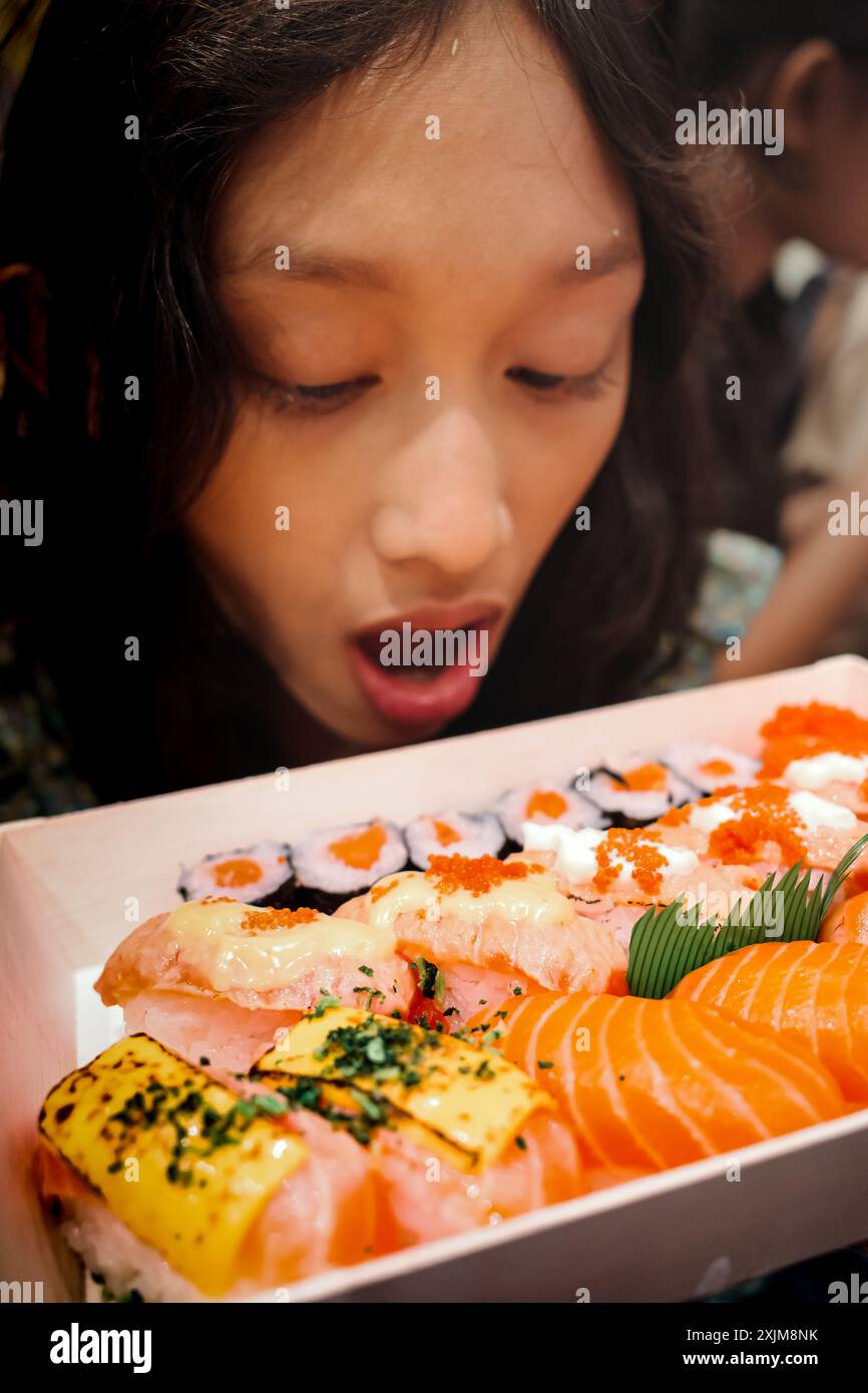 Southeast Asian teenage girl looking at a box of sushi and sashimi ...