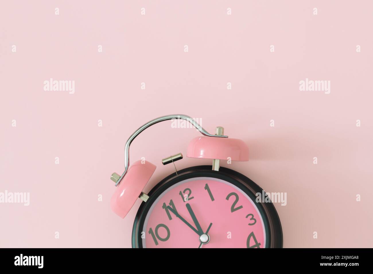 Pastel pink and black alarm clock on light pastel pink background with ...