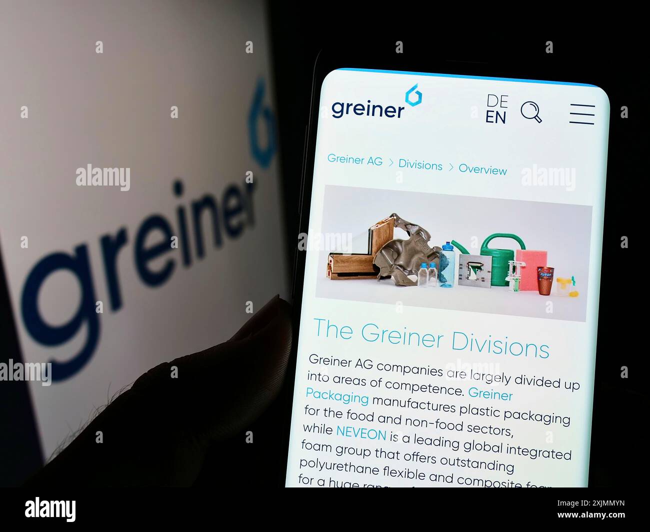 cellphone with webpage of Austrian plastics company Greiner AG on screen in front of logo. Focus ...